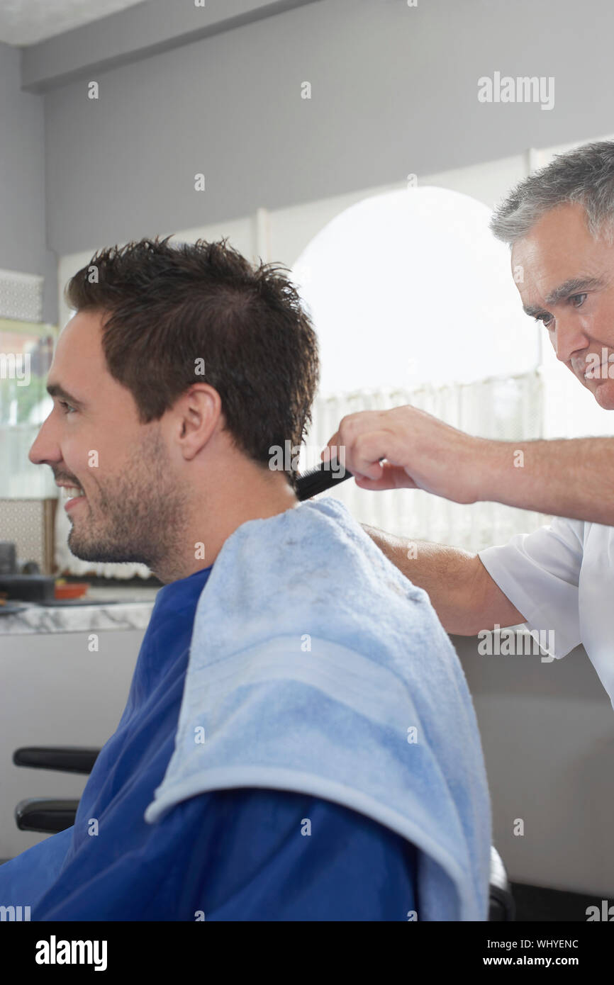 Side view of man getting an haircut from hairdresser in barber shop ...