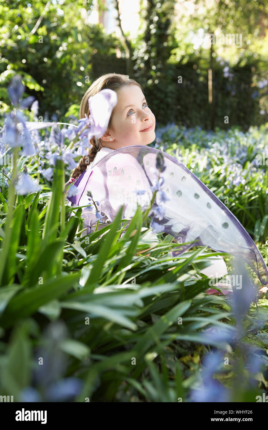 Side view of a cute young girl in fairy costume sitting at flower ...