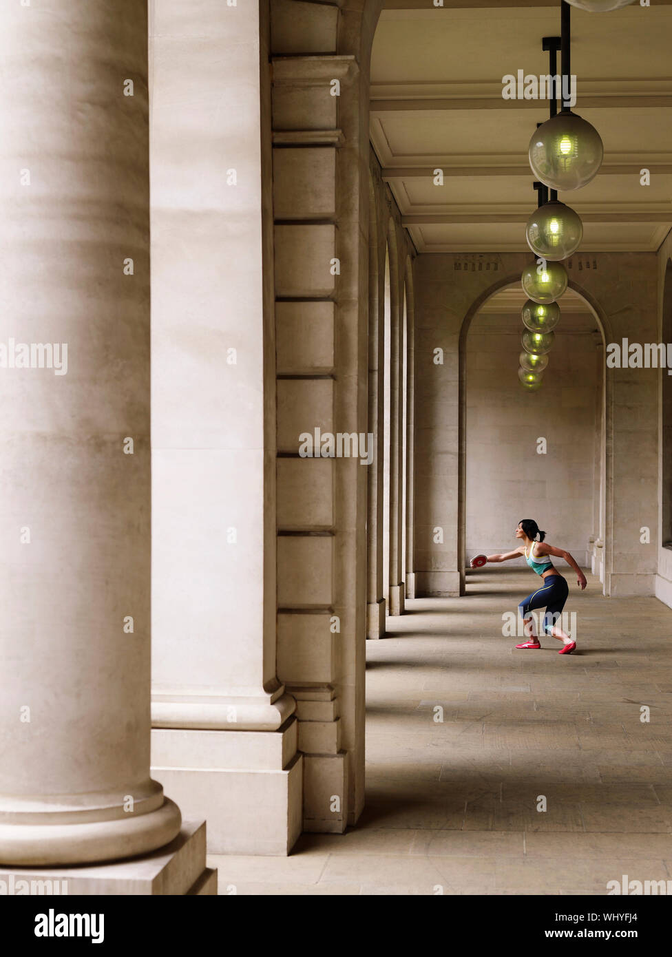 Full length side view of a female athlete throwing discus in portico ...