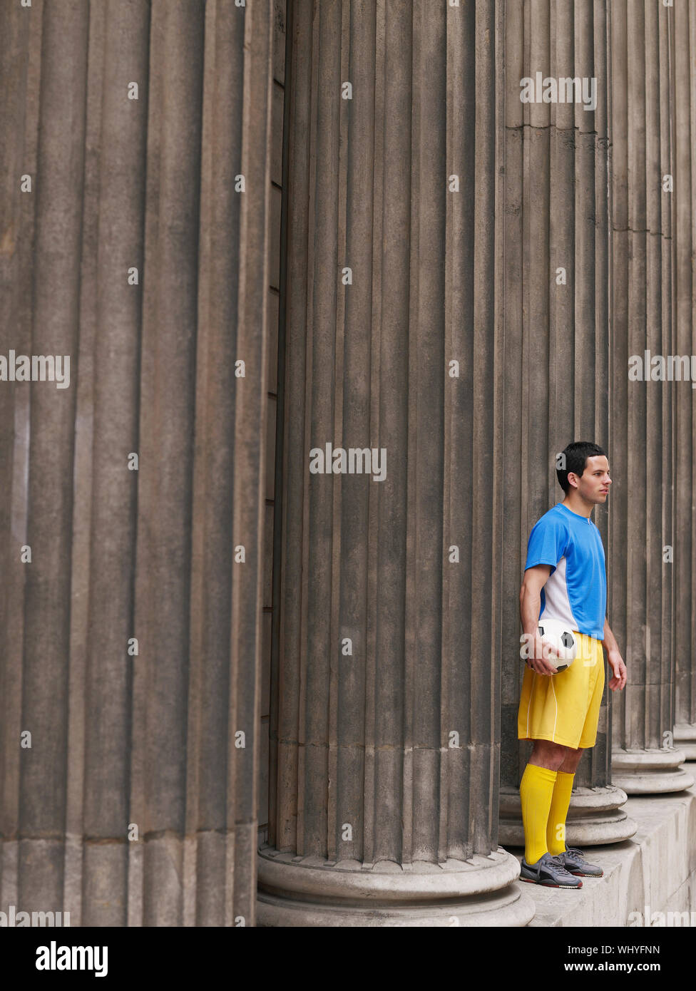 Full length side view of a soccer player holding ball against columns ...