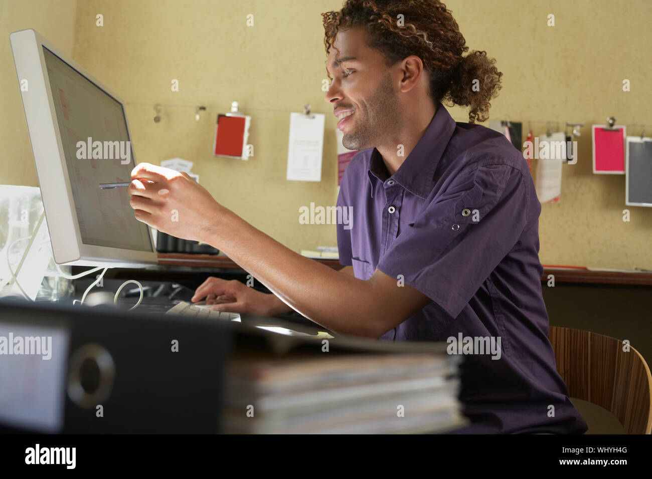 Side view of a smiling young man pointing at computer screen in the ...