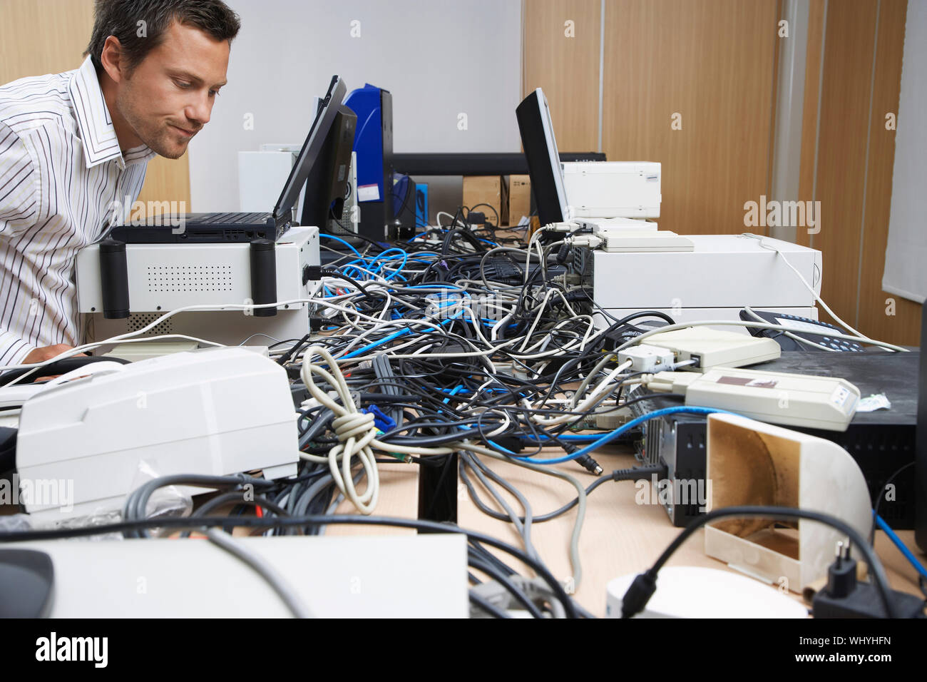 Side view of a male office worker looking at wire mess connecting ...