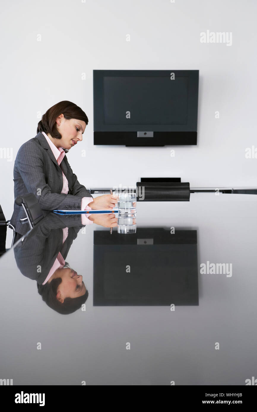 Side view of a young businesswoman writing at table in conference room ...