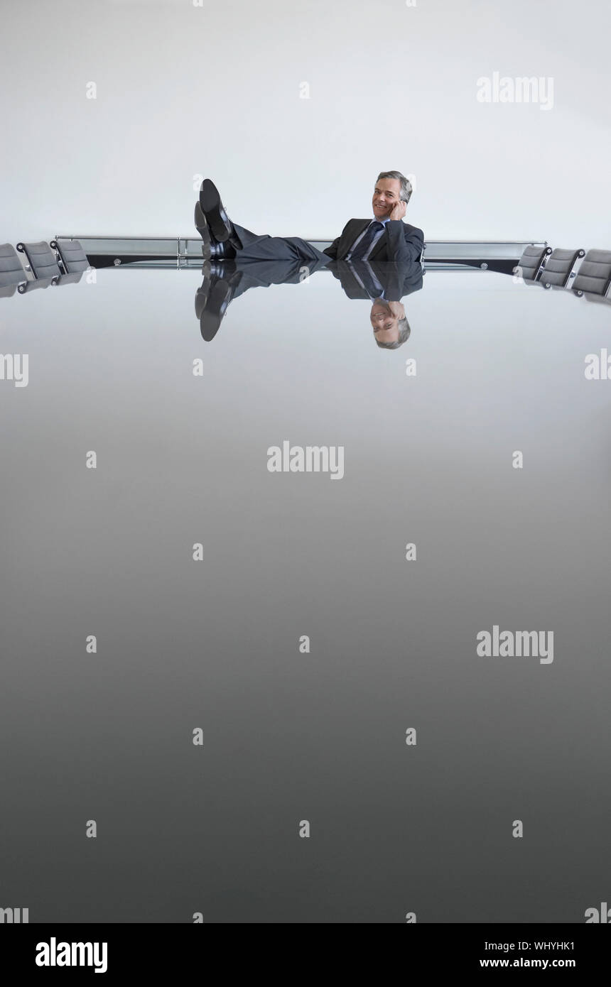 Businessman using cellphone with feet up on table in conference room ...