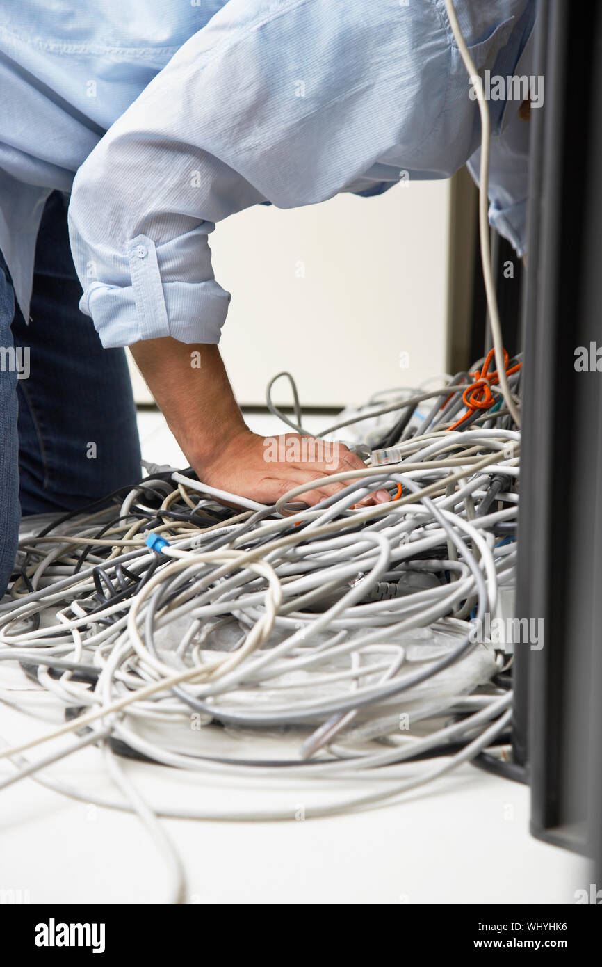 Side view of a man working on tangled computer wires in office Stock ...