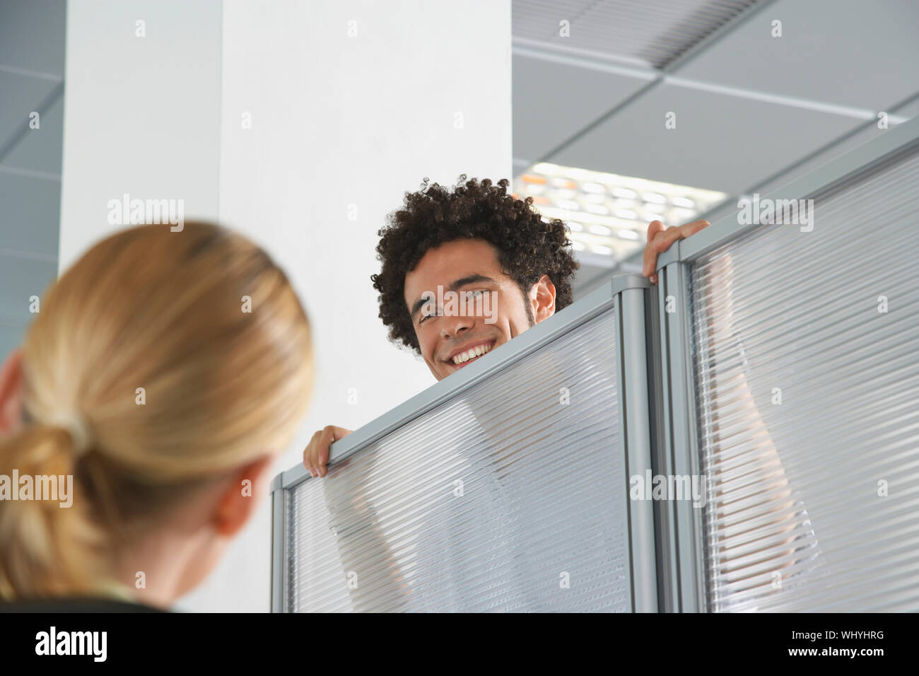 Smiling male office worker peering over cubicle wall to greet blond ...