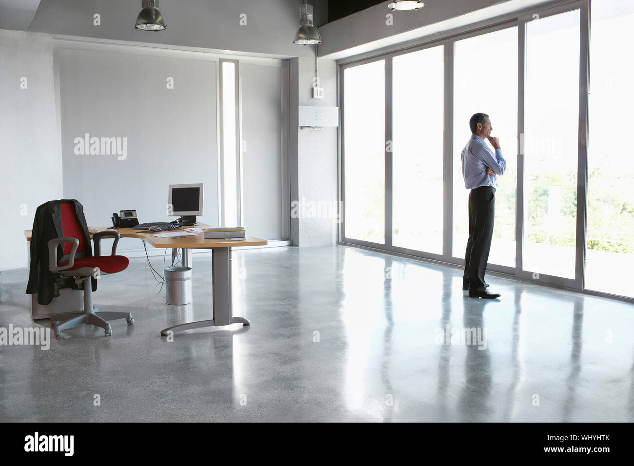 Full length side view of a man looking out of glass door in empty ...