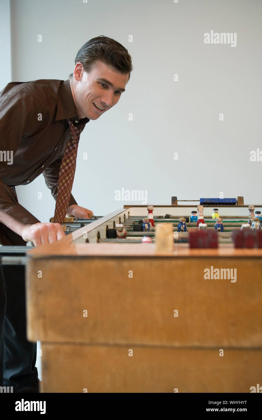Side view of a happy young man playing table football in game room ...