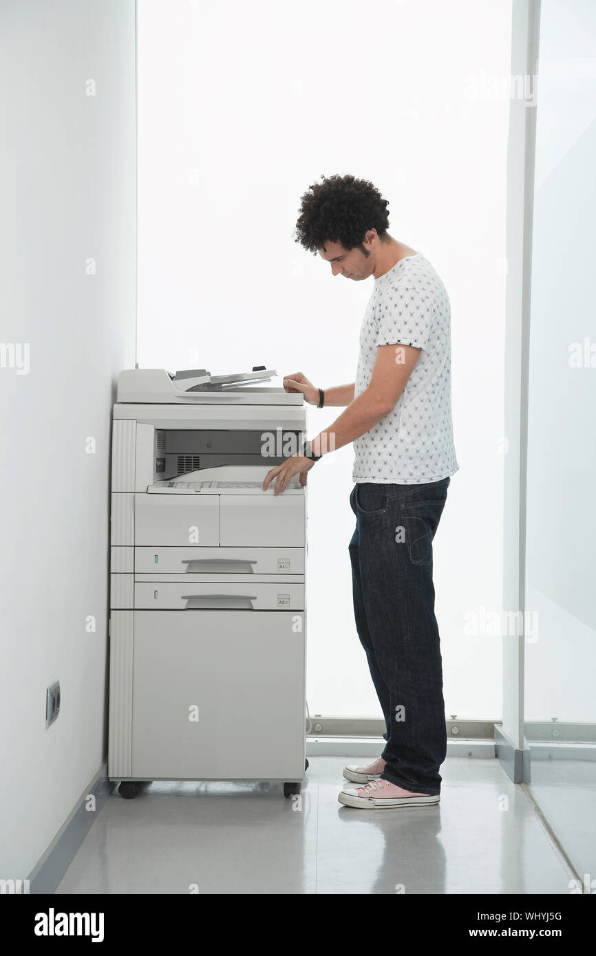 Full length side view of a young man using copy machine in office ...
