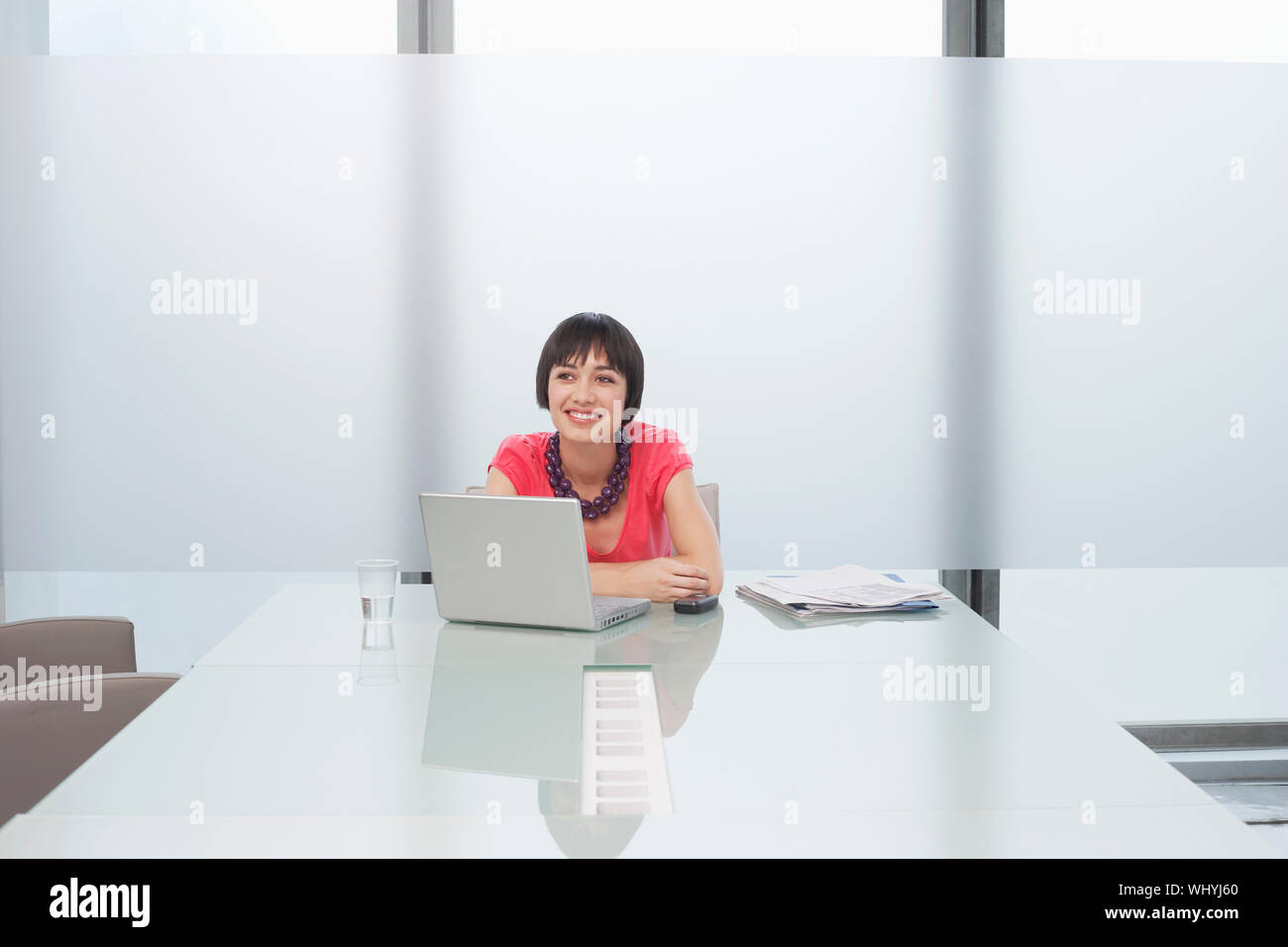 Smiling thoughtful young woman sitting with laptop in modern cubicle at ...