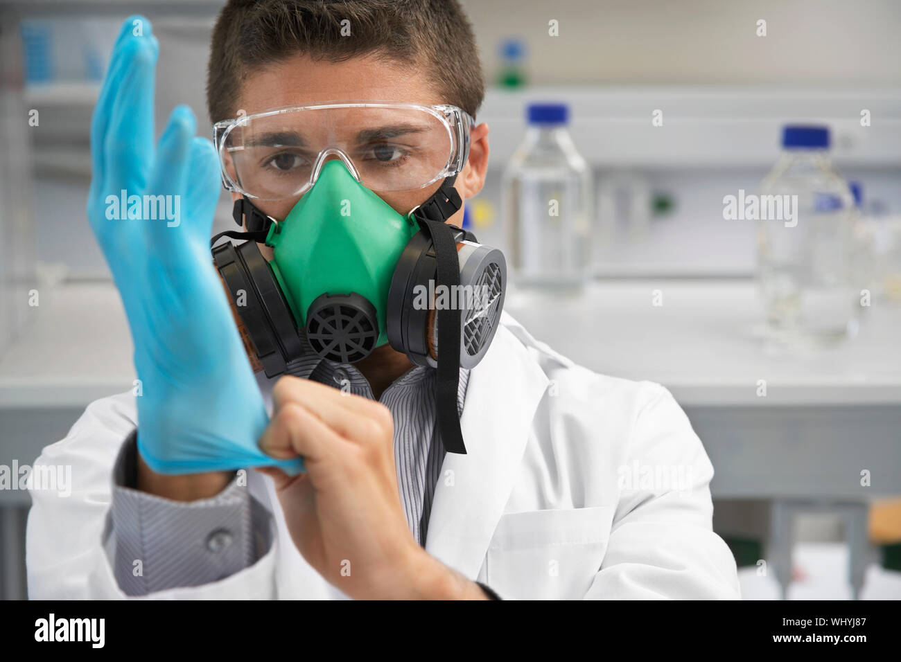 Male scientist in a gas mask while putting on rubber glove in ...