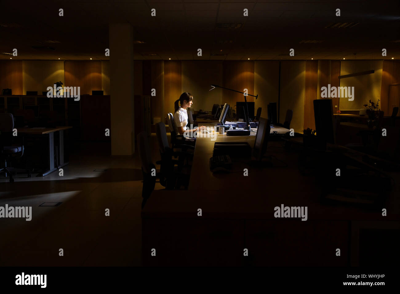 Side view of a young woman working on computer in dark office Stock ...