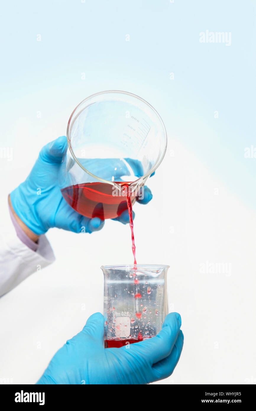 Closeup of gloved hands pouring red liquid into beaker against white ...