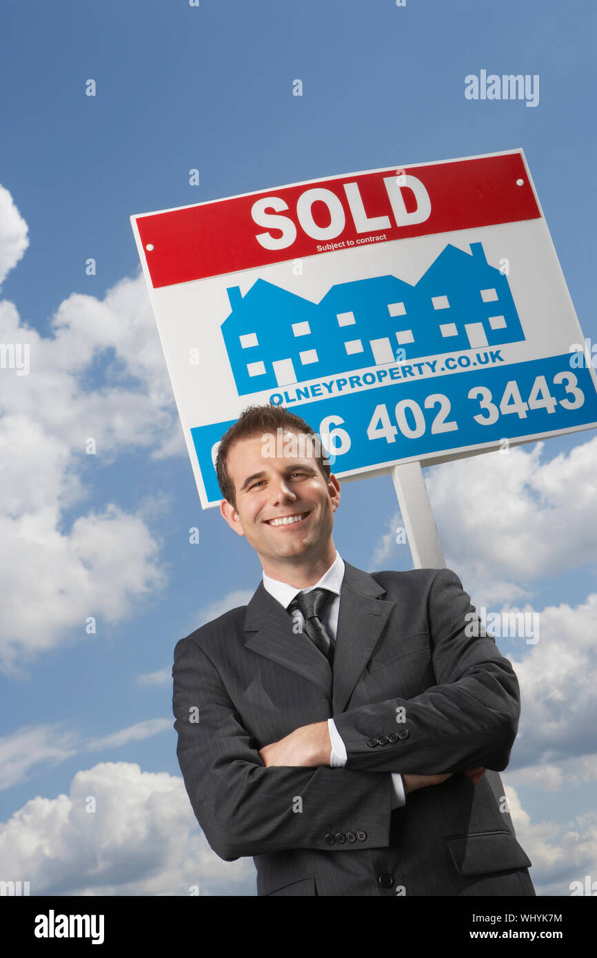 Low angle portrait of a smiling male real estate agent in front of sold ...