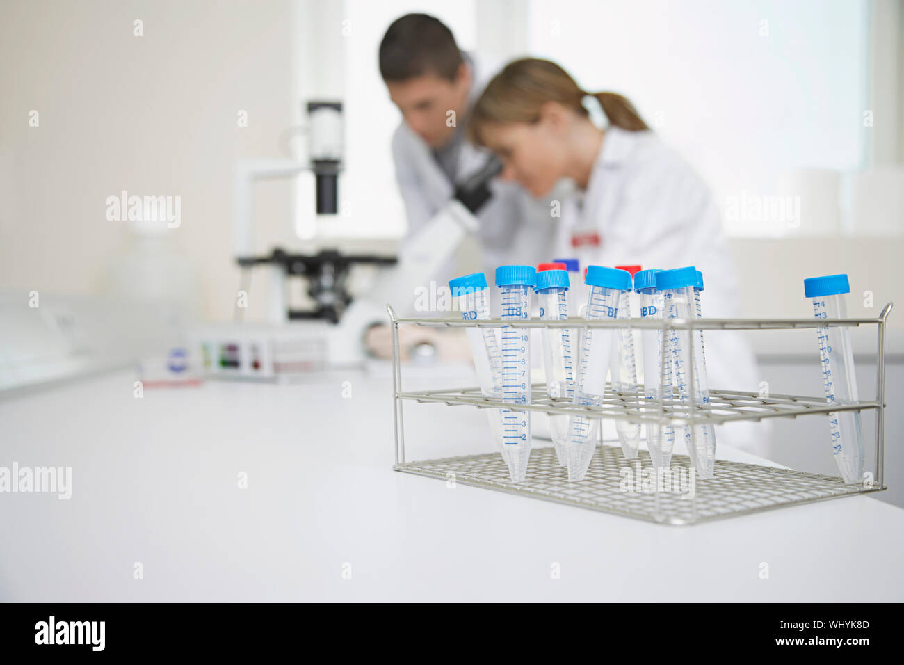 Side view of scientists looking in microscope with test tubes in focus ...