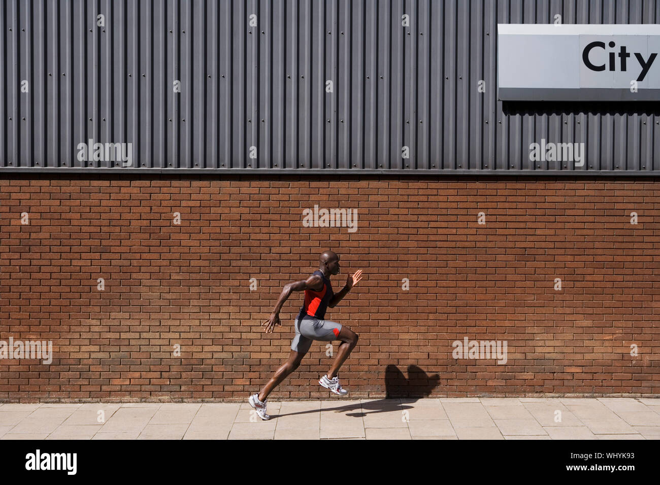 Side view of a man running past brick wall with 'city' written on it ...