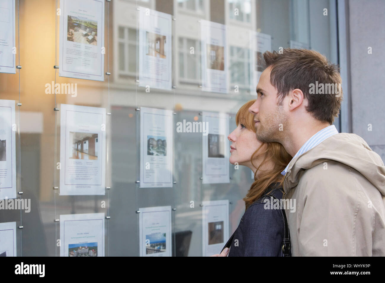 Side view of a young couple looking at window display at real estate ...