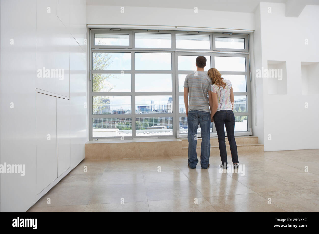 Full length rear view of an affectionate couple looking out of window ...