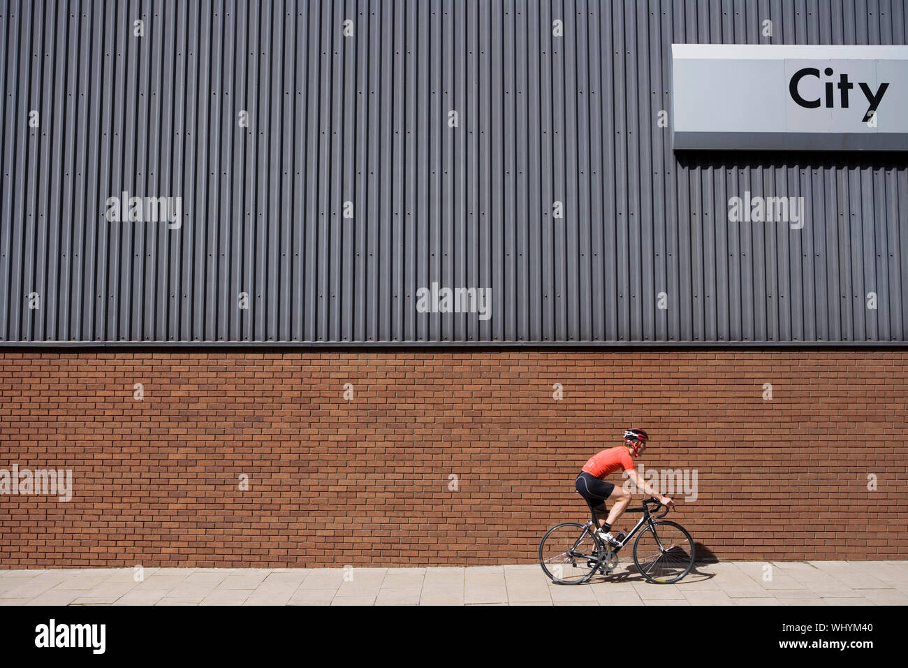 Side view of a man cycling past building with 'City' written on side ...