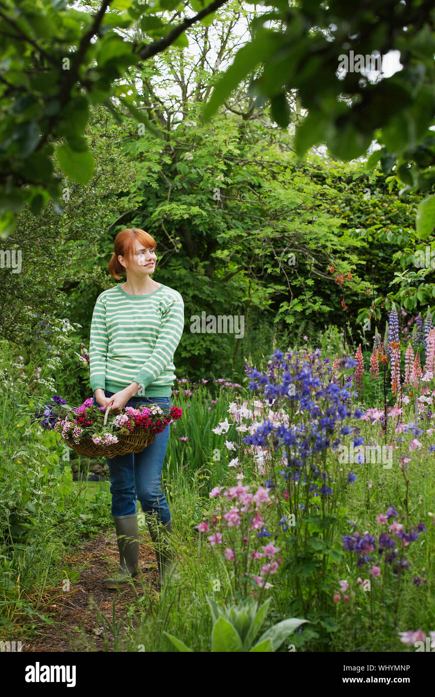 Full length of a smiling young woman carrying basket of flowers in ...