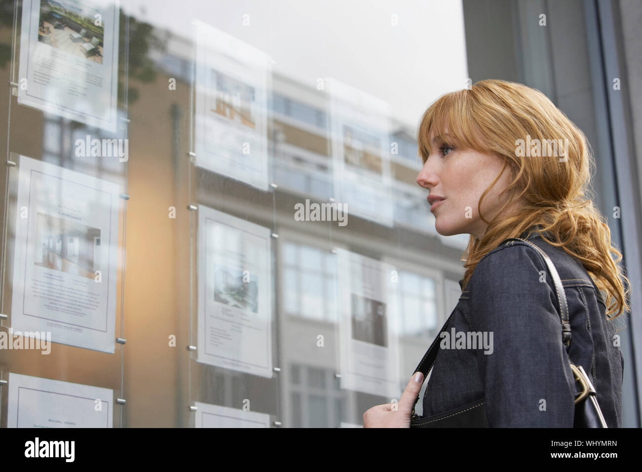 Side view of a young woman looking at window display at real estate ...