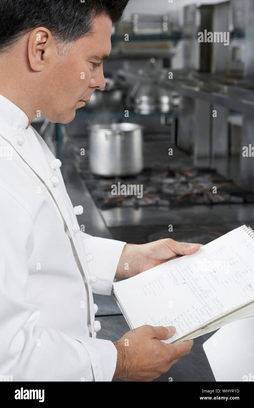 Side view of a middle aged male chef reading recipe book in the kitchen ...