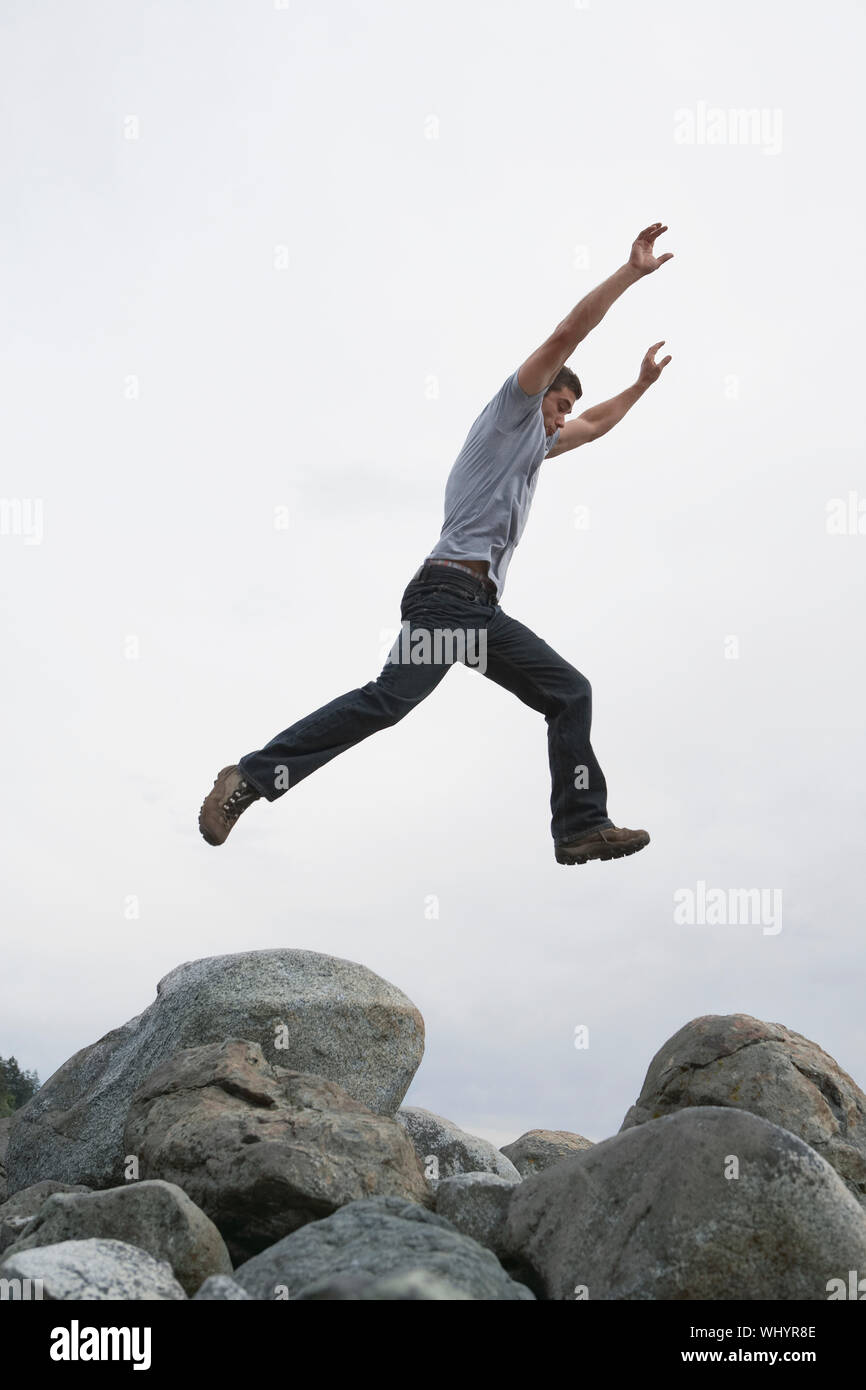 Full length low angle view of a young man jumping with arms raised over ...