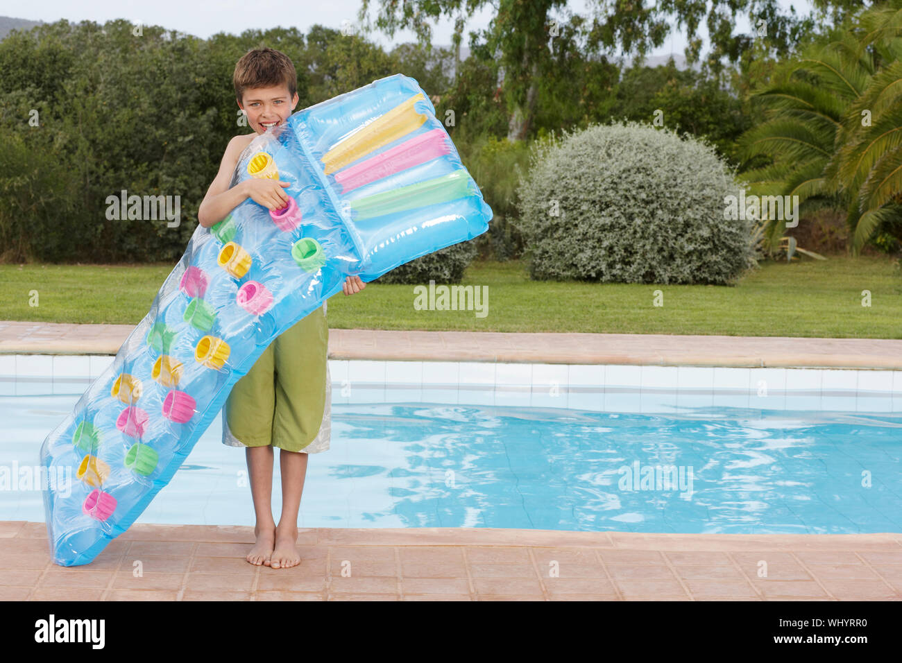 Full length of a young boy blowing up air mattress against the pool ...