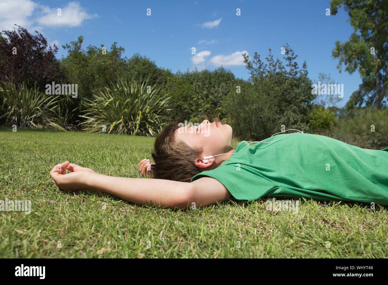 Side view of a young boy resting on grass and listening to MP3 player ...