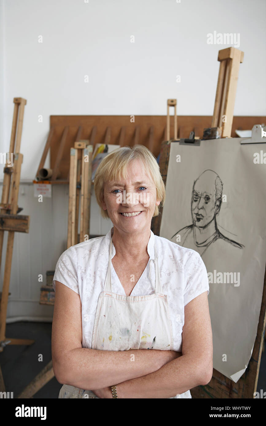 Portrait of a smiling mature female artist standing by artwork in ...