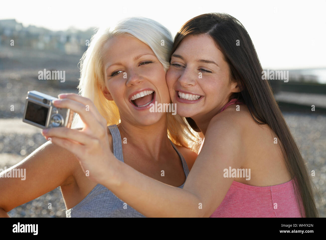 Cheerful female friends with cheek to cheek photographing themselves at ...