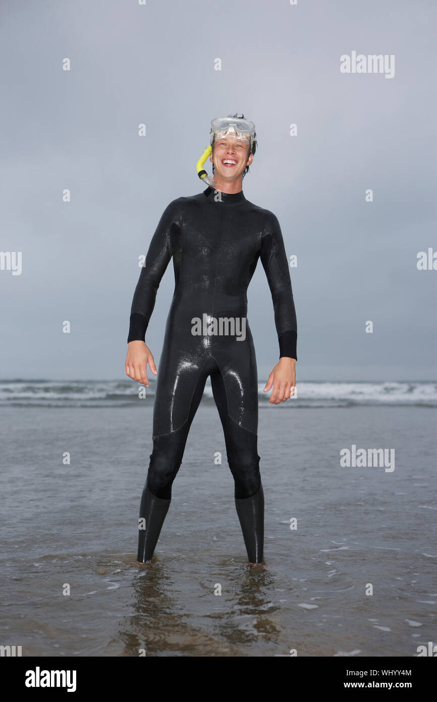 Happy young man wearing wetsuit while standing in water at beach Stock ...