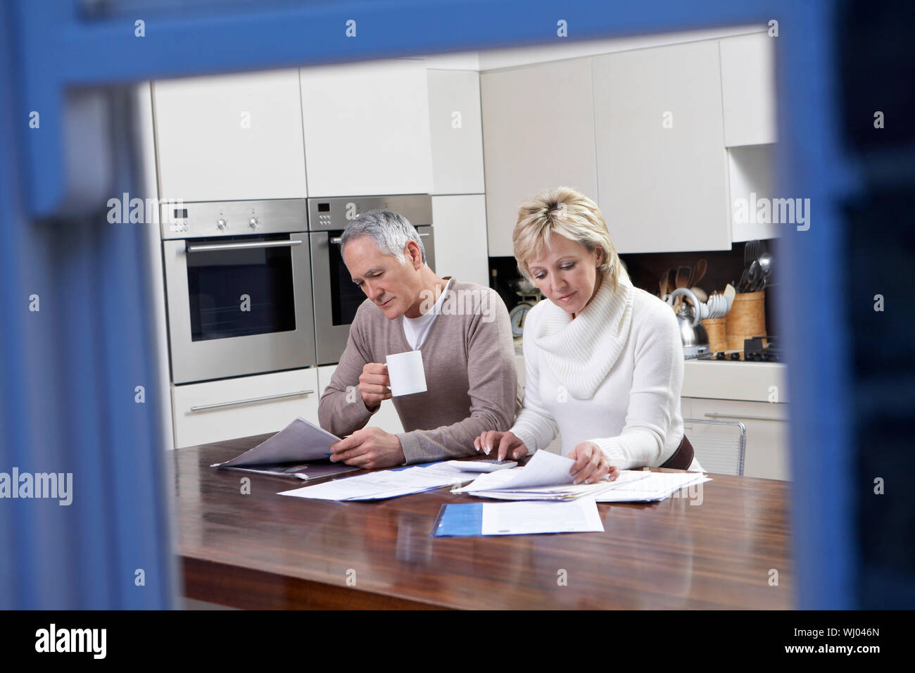 Middle aged couple calculating their domestic bills at kitchen table ...