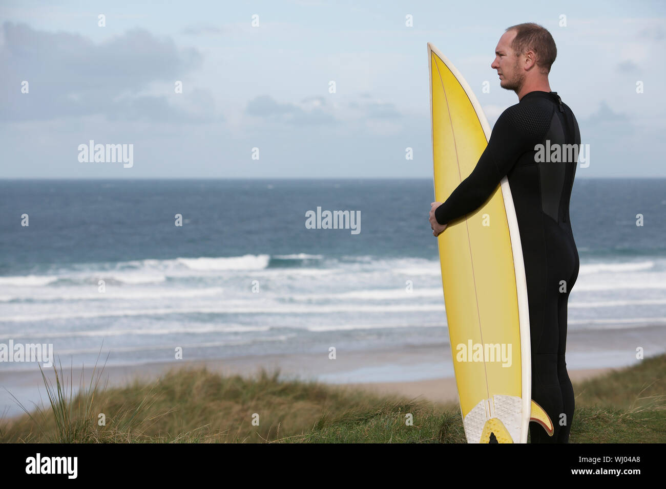 Side view of male surfer carrying surfboard on beach looking at sea ...