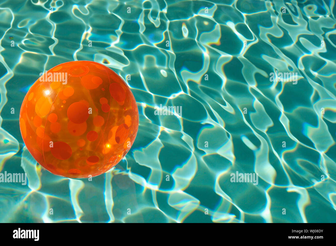 Orange inflatable beach ball floating in pool Stock Photo - Alamy
