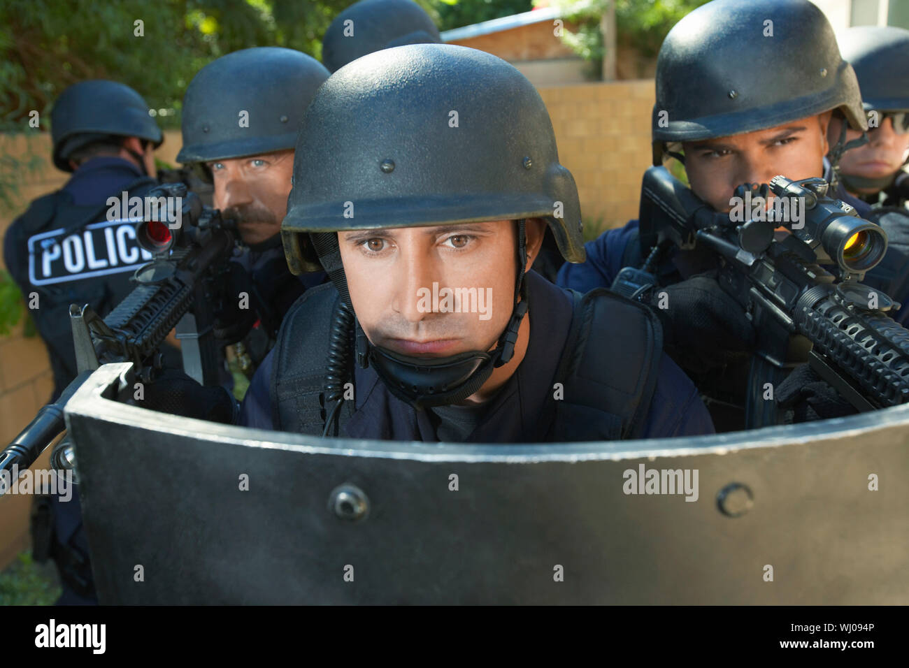 Policeman aiming with gun by coworker behind shield Stock Photo - Alamy