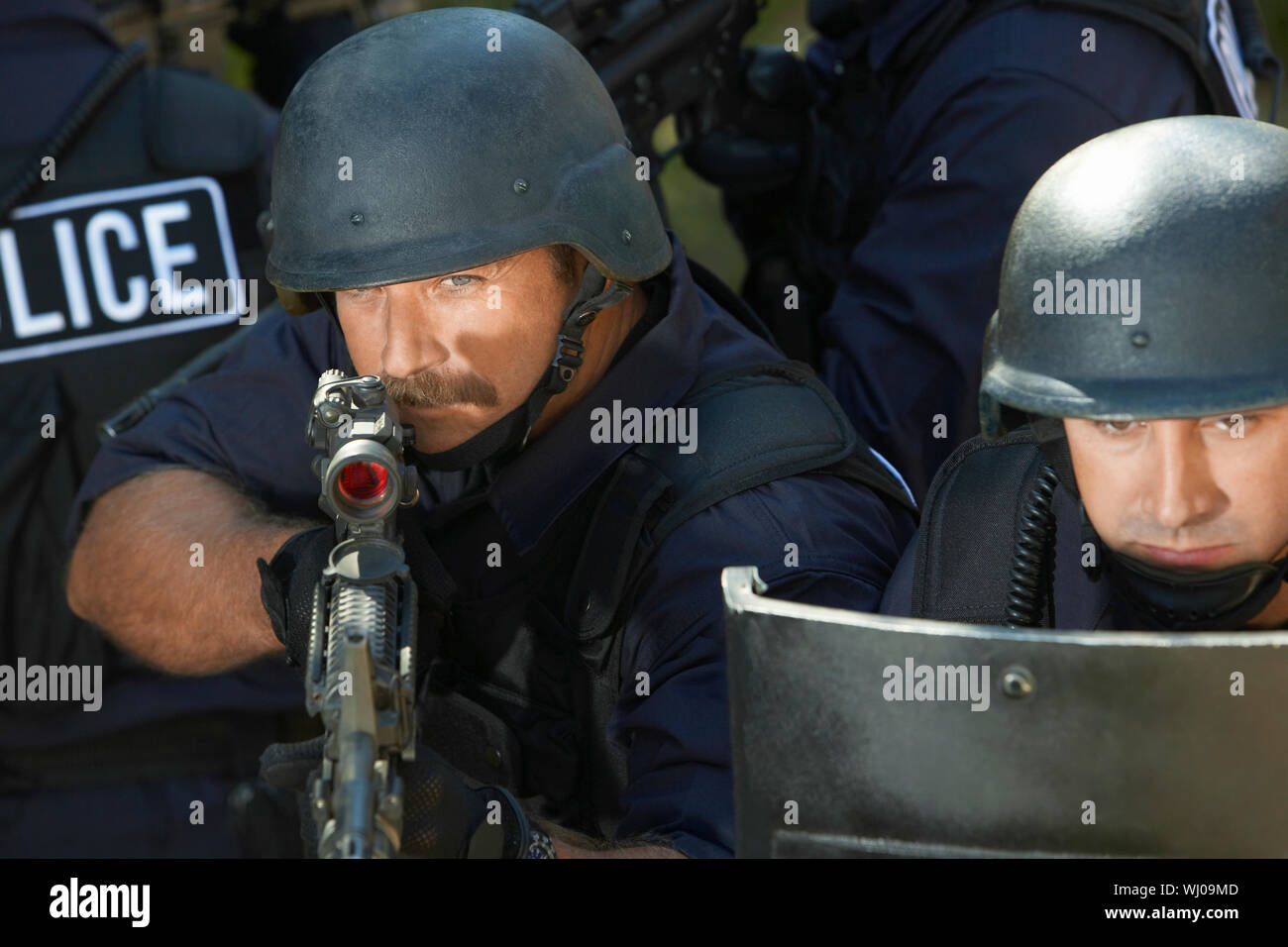 Policeman aiming with gun by coworker behind shield Stock Photo - Alamy