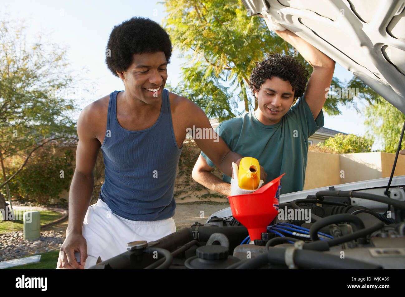 Two young men pouring oil into car engine Stock Photo - Alamy