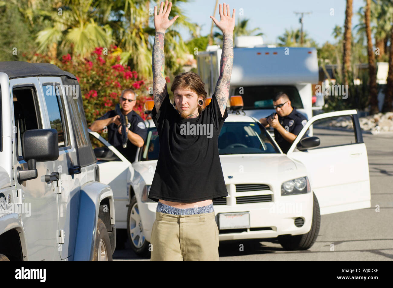 Portrait of a young man surrendering with two police officers aiming ...