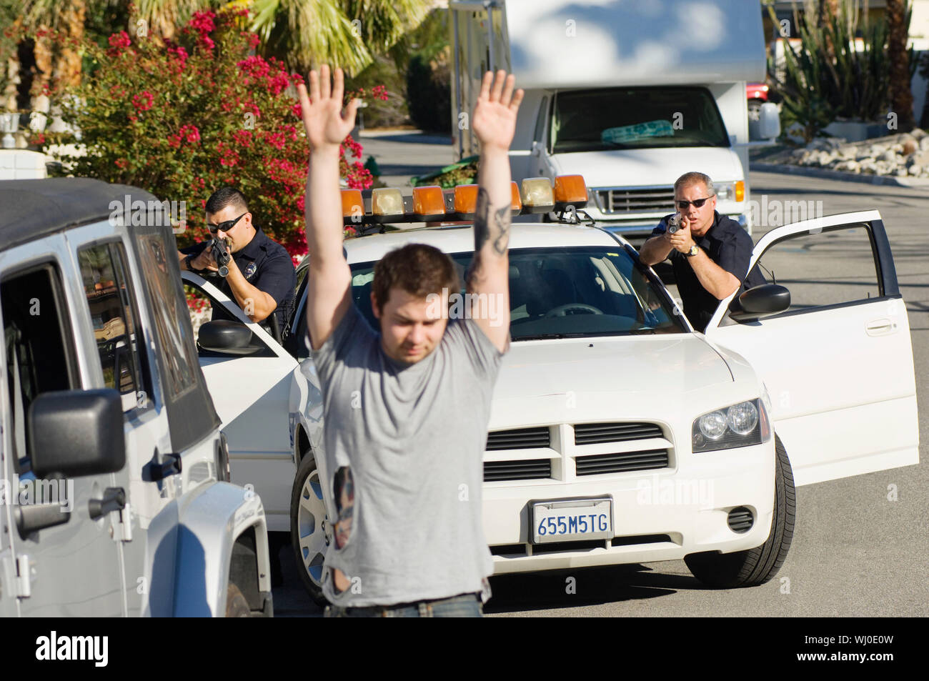 A young man surrendering with two police officers aiming gun at him ...