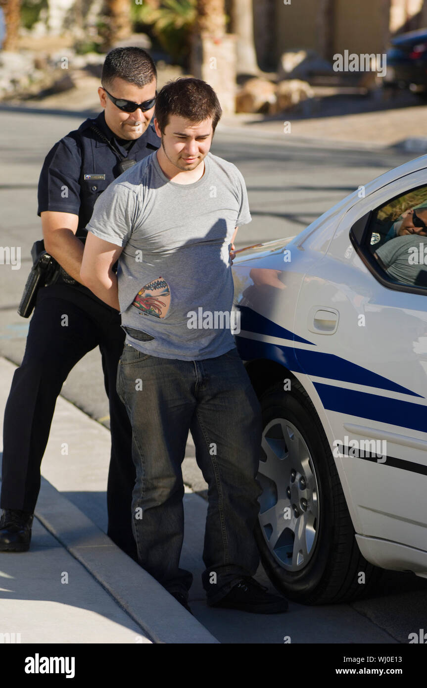 Full length of a police officer arresting young man for breaking ...