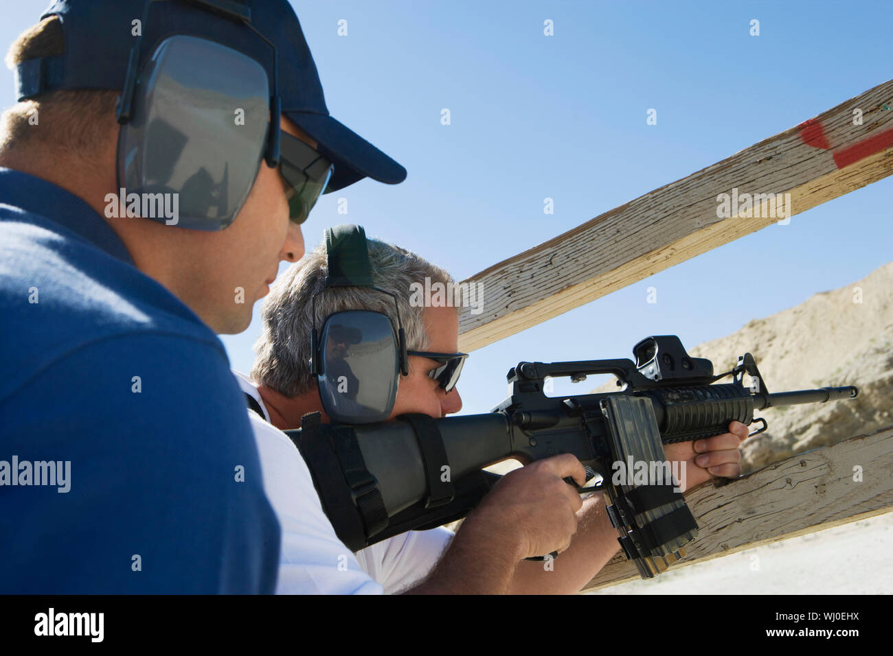 Instructor with man aiming machine gun at firing range, low angle view ...