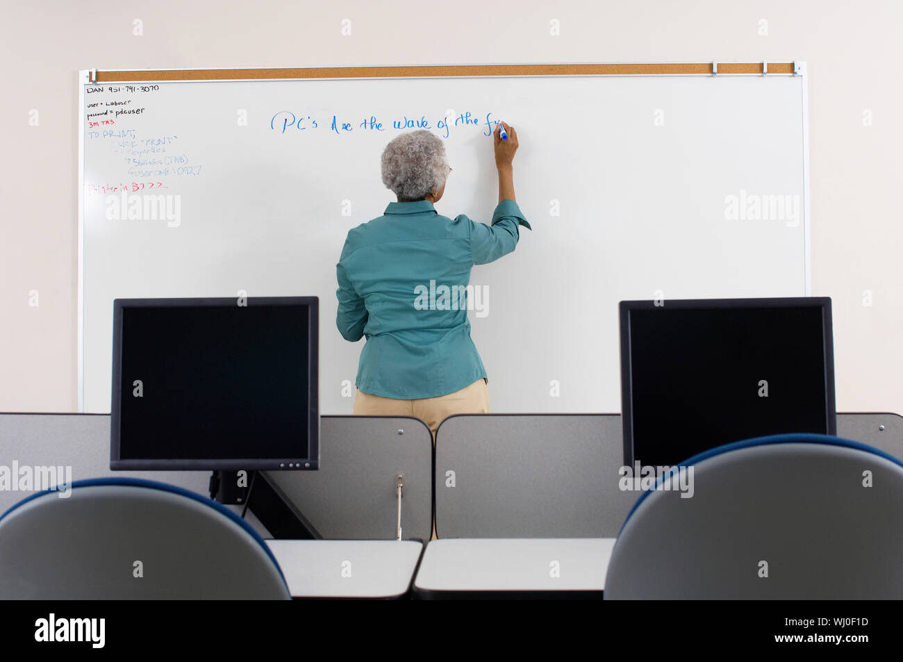 Female teacher writing on whiteboard in computer classroom Stock Photo ...