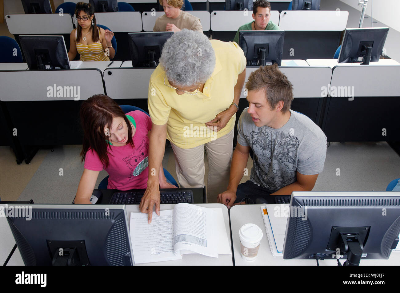 Teacher helping two students working in computer classroom Stock Photo ...