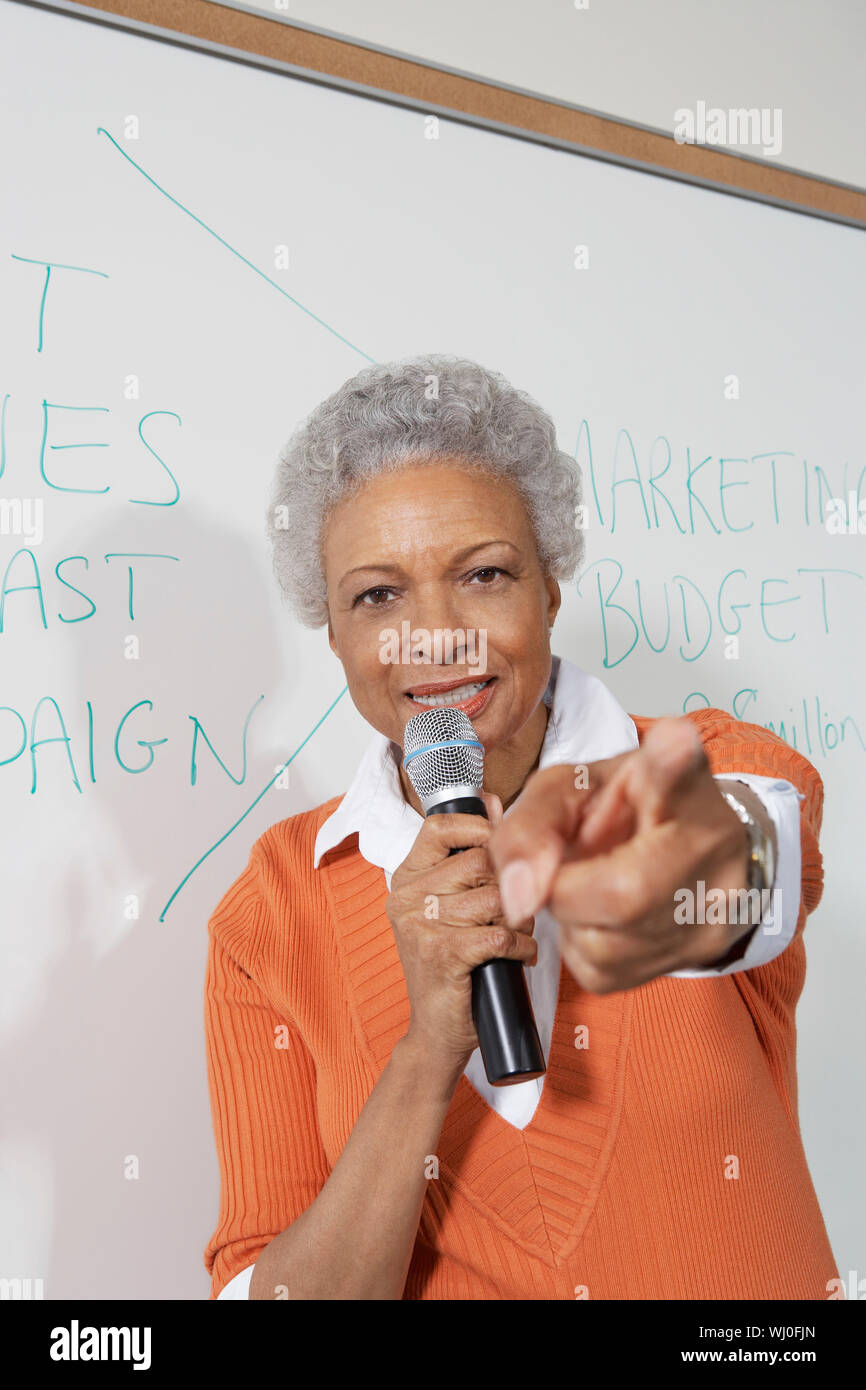 Female teacher using microphone, pointing near white board Stock Photo ...