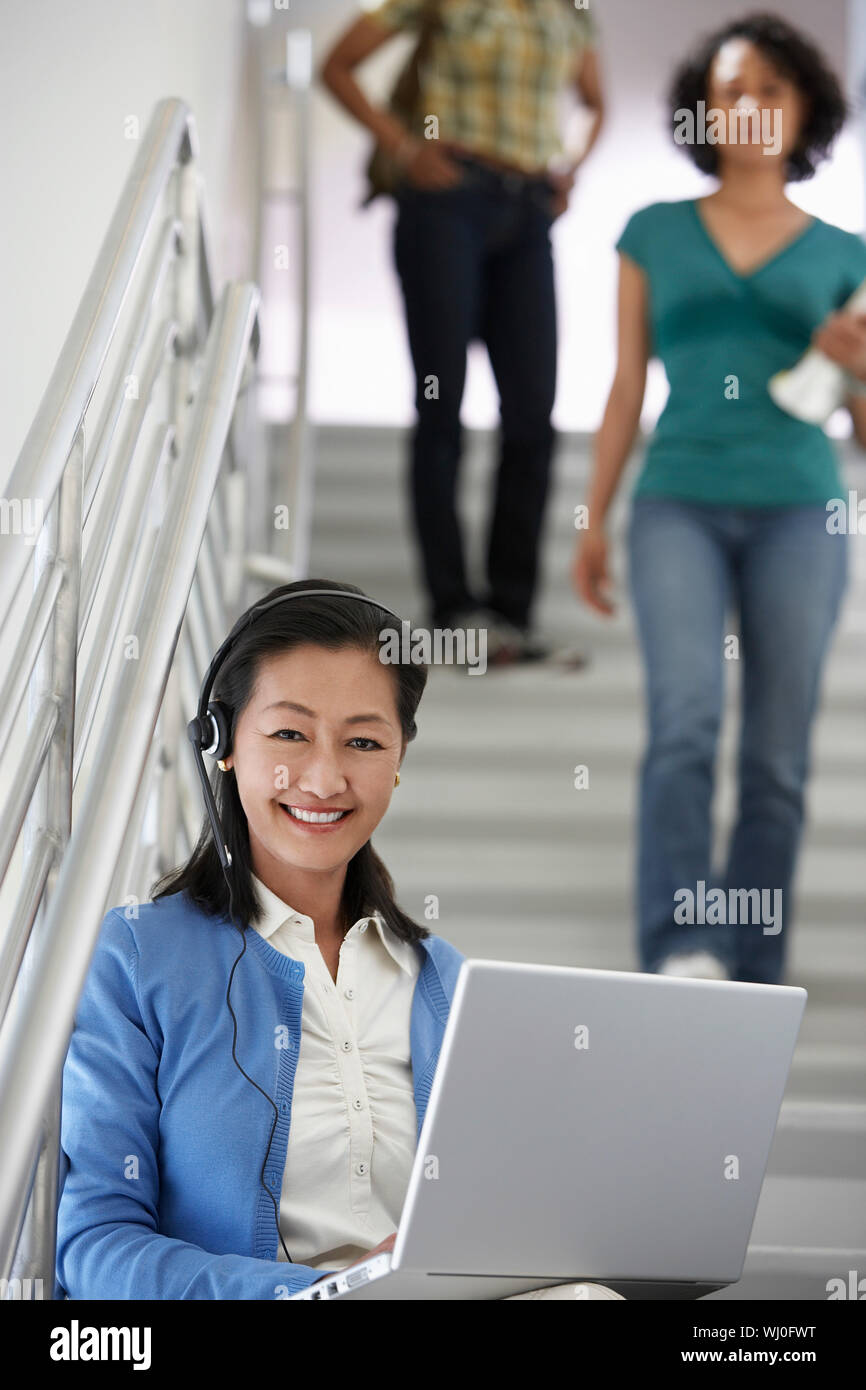 Teacher using laptop on stairs in school, students in background Stock ...