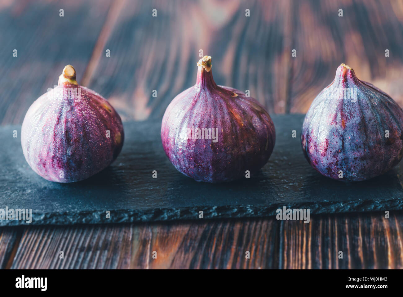 Three fresh figs on the black stone board Stock Photo - Alamy