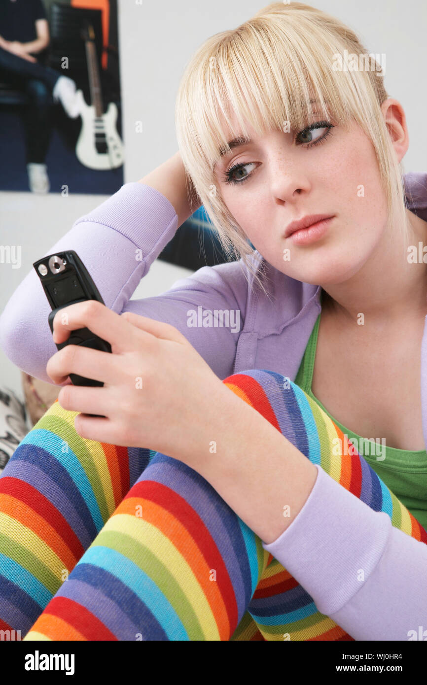 Beautiful teenage girl reading text message on mobile phone at home ...