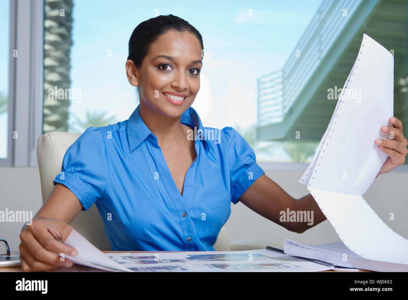 Portrait of a happy female Indian estate agent looking at building ...