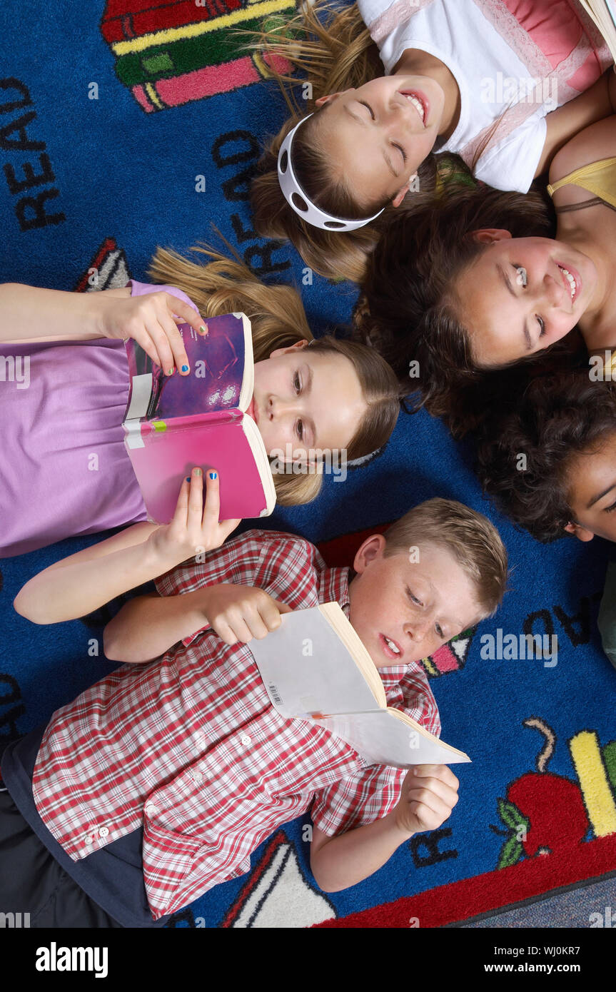 School children reading books on floor in library Stock Photo - Alamy